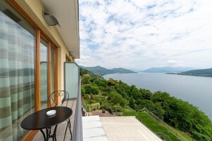 Varanda com mesa e cadeiras, vista para um lago e montanhas ao longe.
