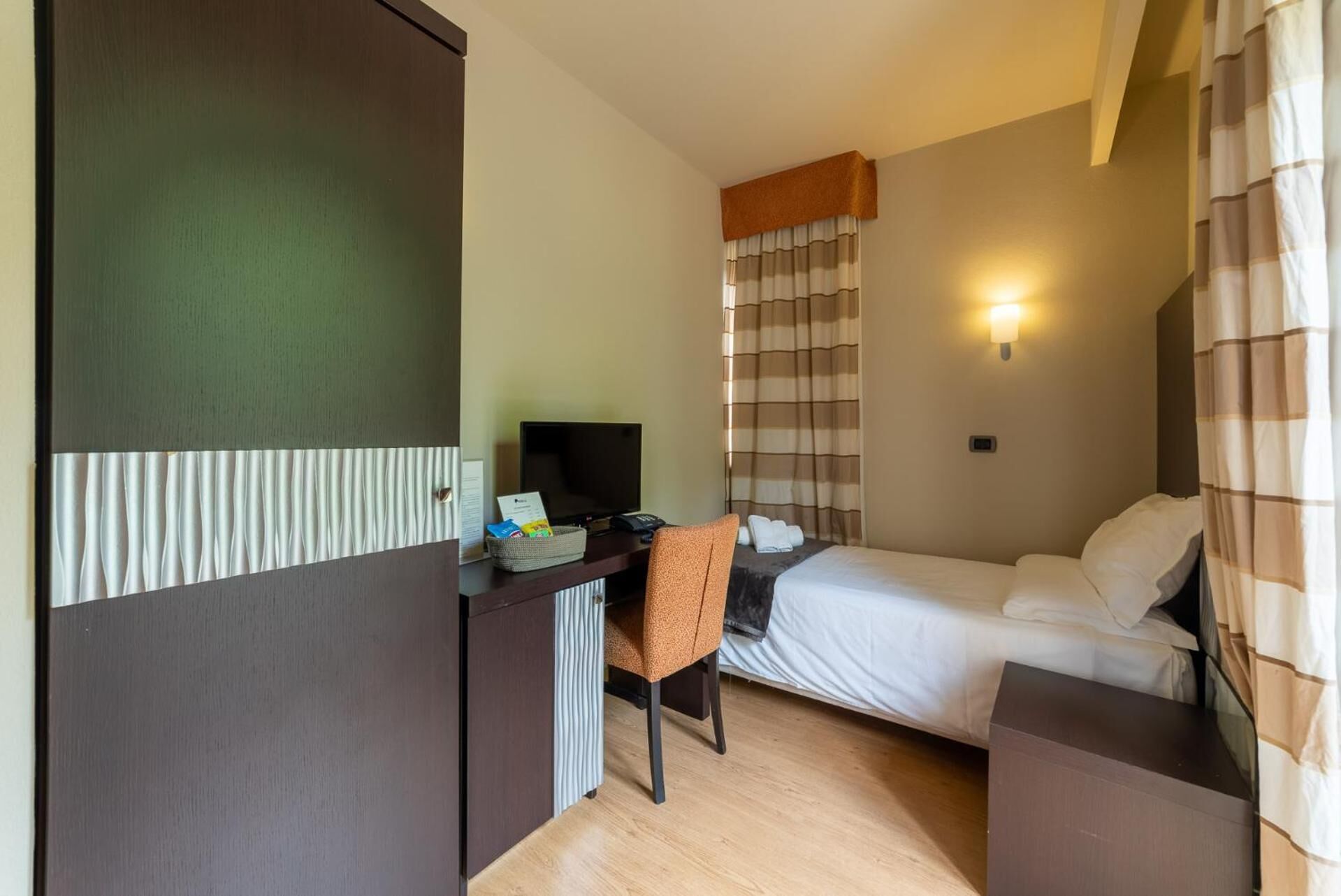 Quarto de hotel com uma cama, uma mesa com computador, uma cadeira e uma televisão.