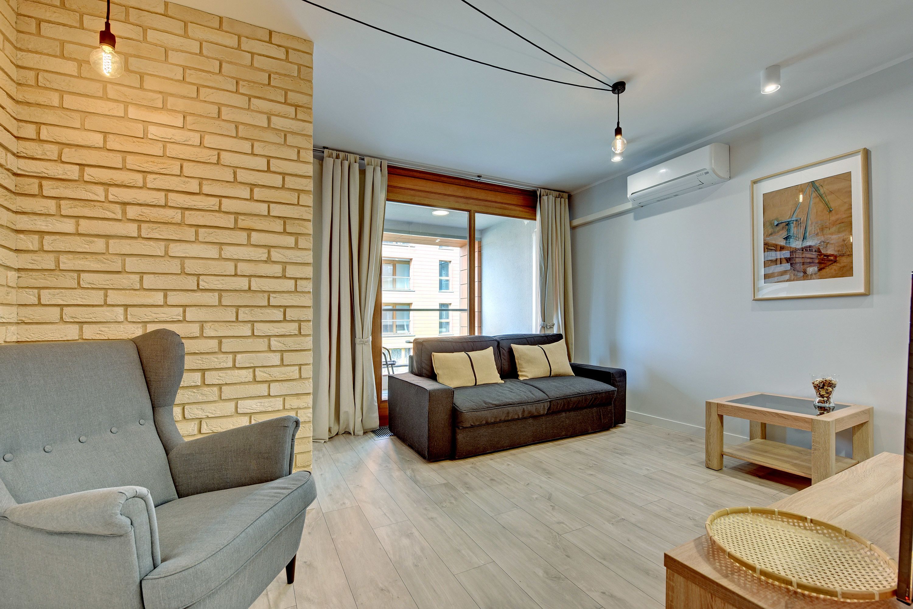 Uma sala de estar moderna com parede de tijolos, um sofá cinzento, uma pequena mesa de madeira e uma cesta de vime.