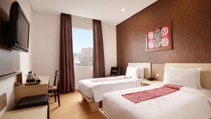 Quarto de hotel com duas camas, uma escrivaninha, uma cadeira, televisão e janela com cortinas.