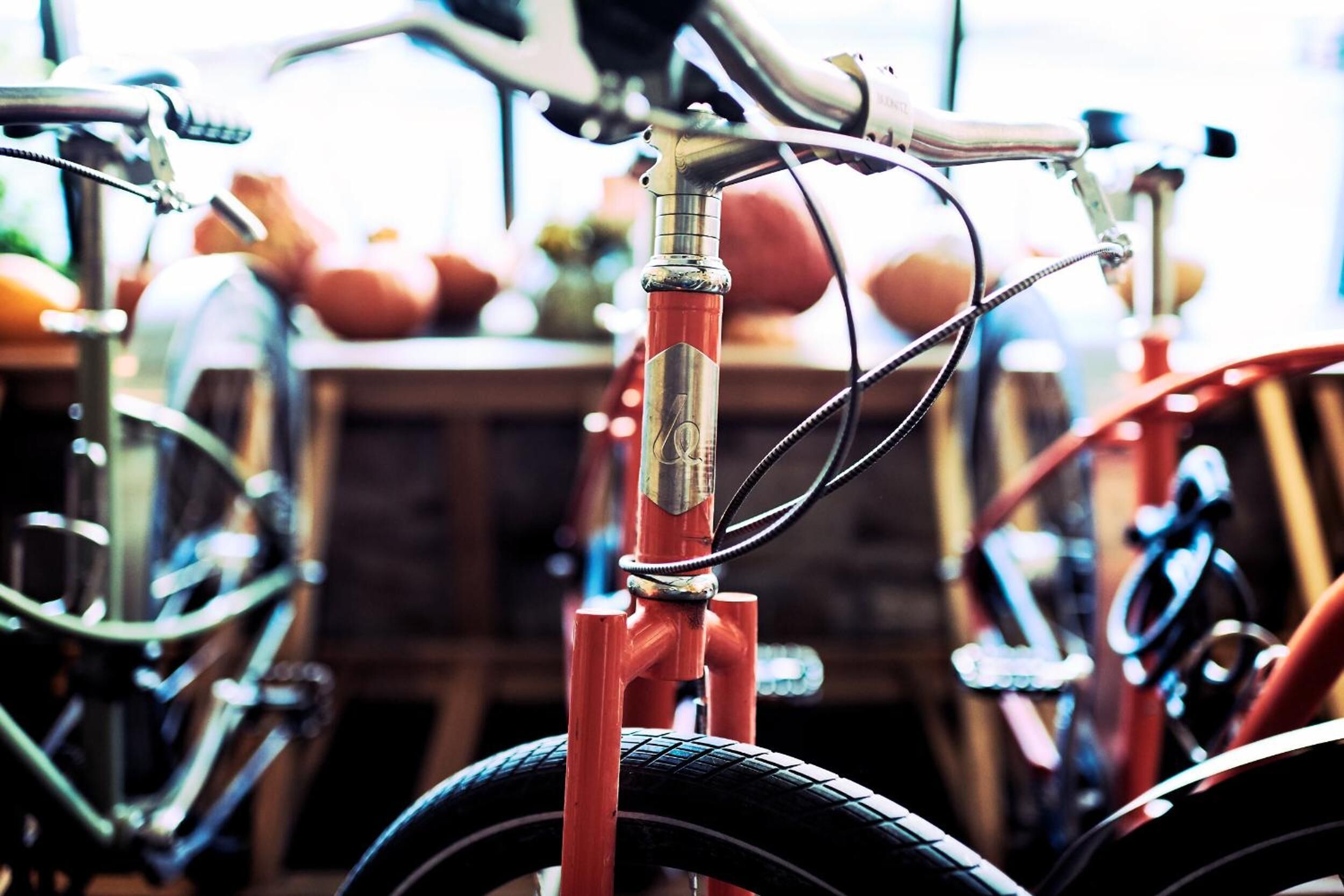 Detalhe do guidão e garfo dianteiro de uma bicicleta, com outras bicicletas desfocadas ao fundo.