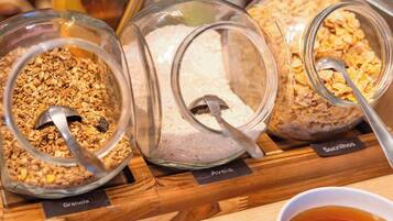 Três recipientes de vidro etiquetados com diferentes tipos de granola sobre uma superfície de madeira.