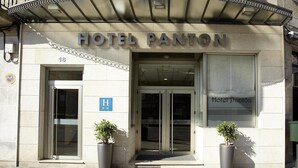 Entrada do Hotel Pantón com placa visível, símbolo de acessibilidade para cadeiras de rodas e dois vasos de plantas na entrada.