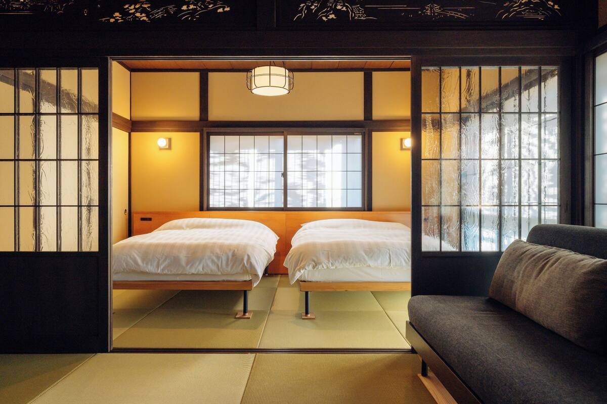Um quarto japonês tradicional com tatames, duas camas, um sofá e portas corrediças com biombos shoji.