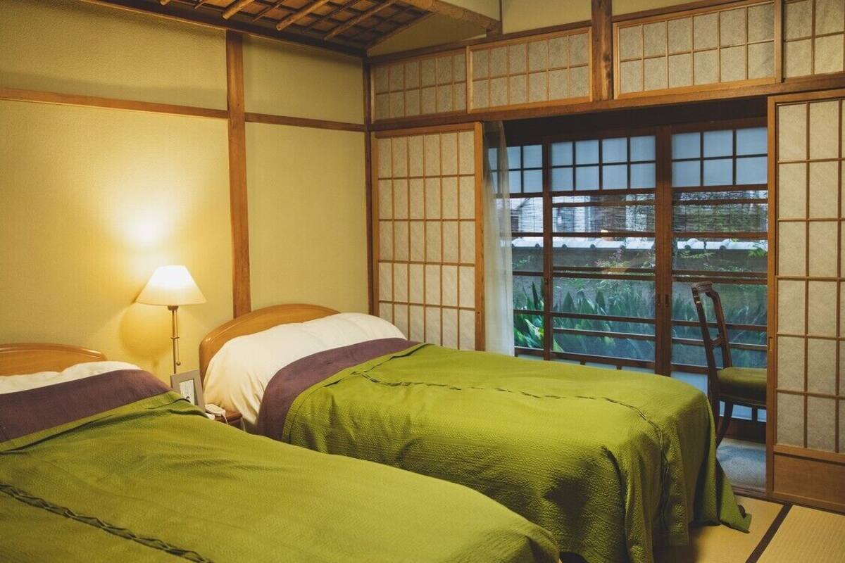 Quarto tradicional japonês com piso de tatame, divisória shoji e duas camas com roupa de cama verde.