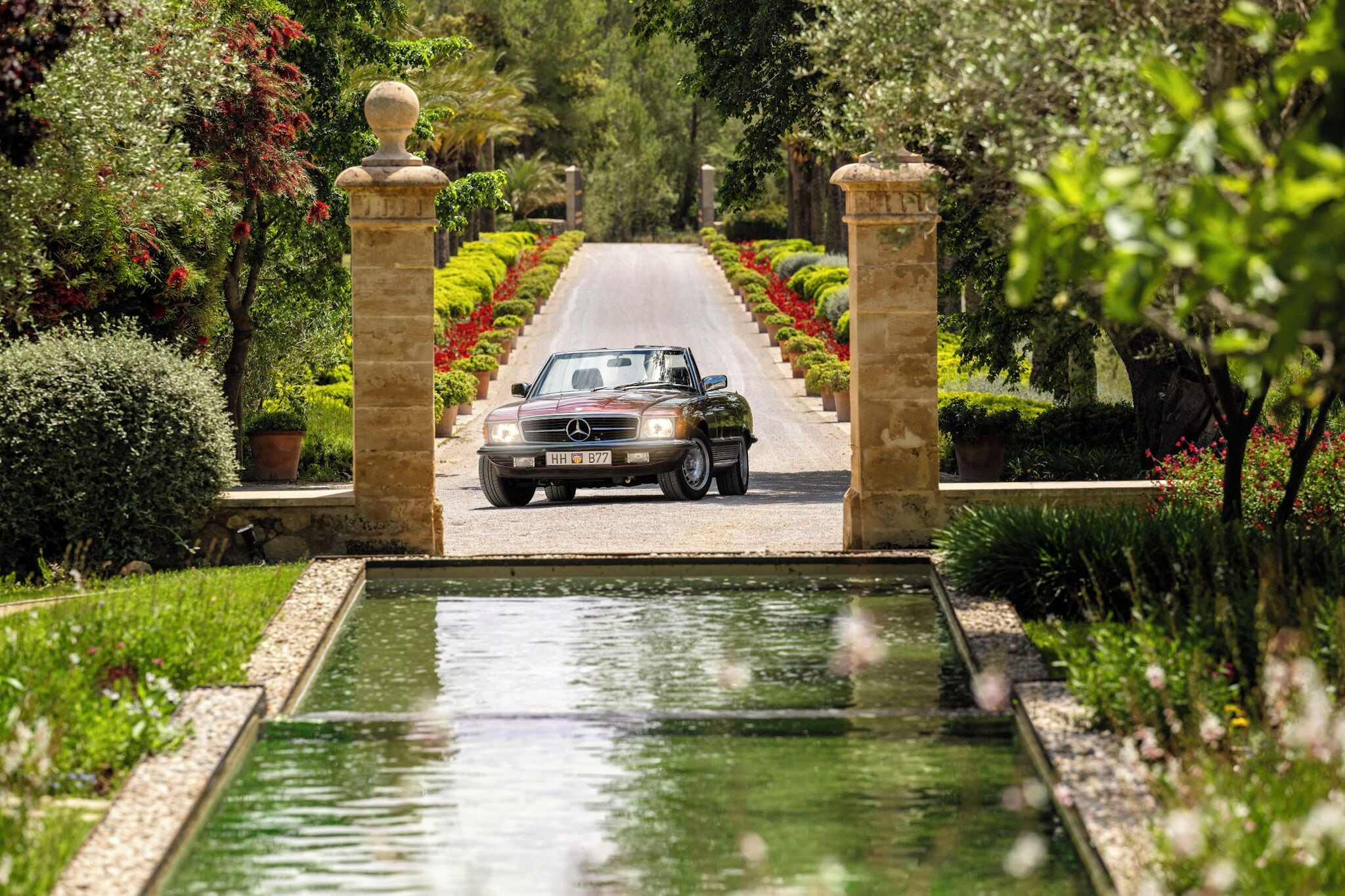 Um carro passando por um jardim com um espelho d'água e pilares de pedra.