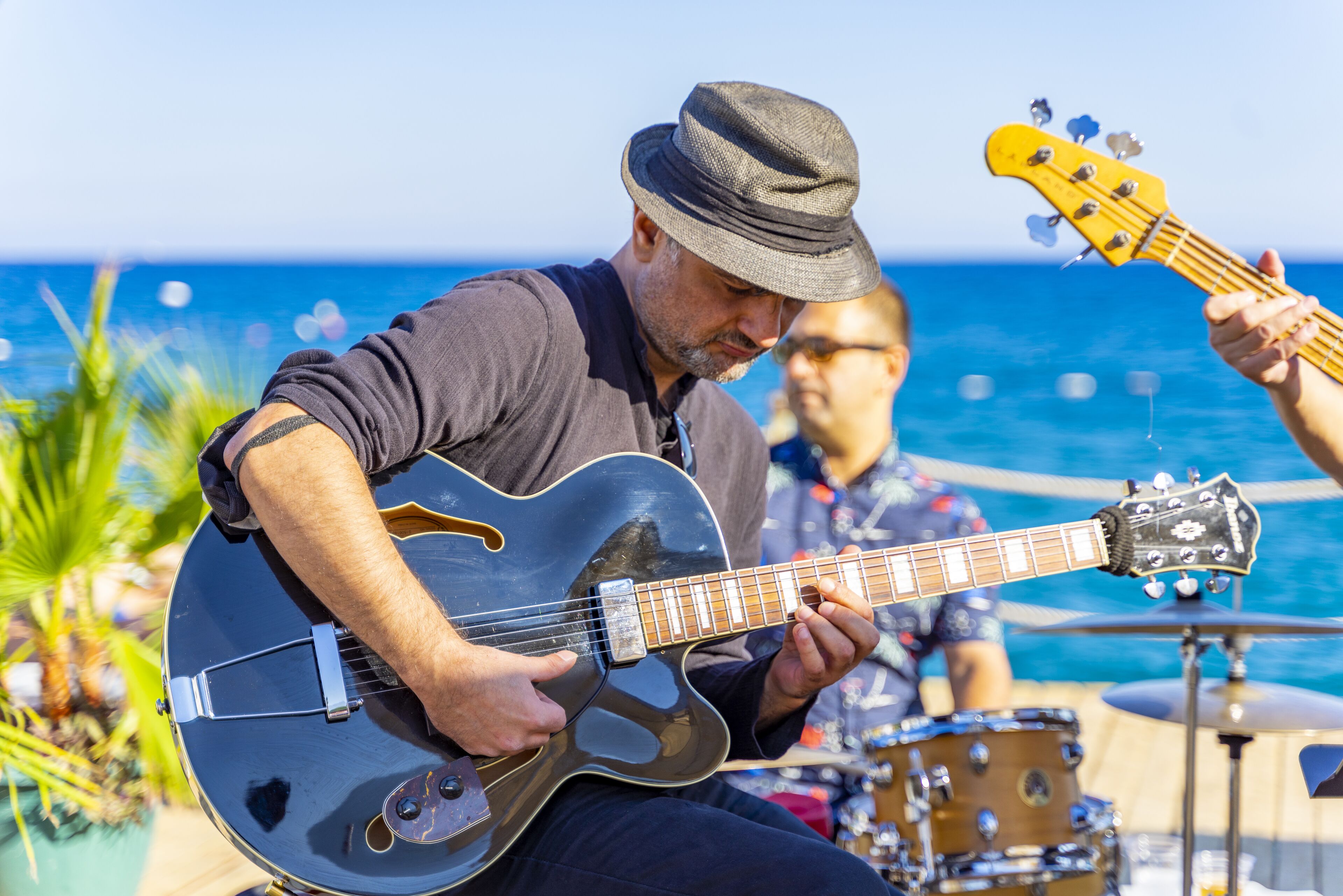 Uma pessoa tocando uma guitarra elétrica preta ao ar livre, com uma vista desimpedida do oceano ao fundo.