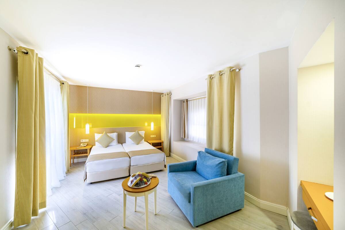 Quarto de hotel com uma cama, um sofá azul, uma mesinha e uma mesaninha de cabeceira.