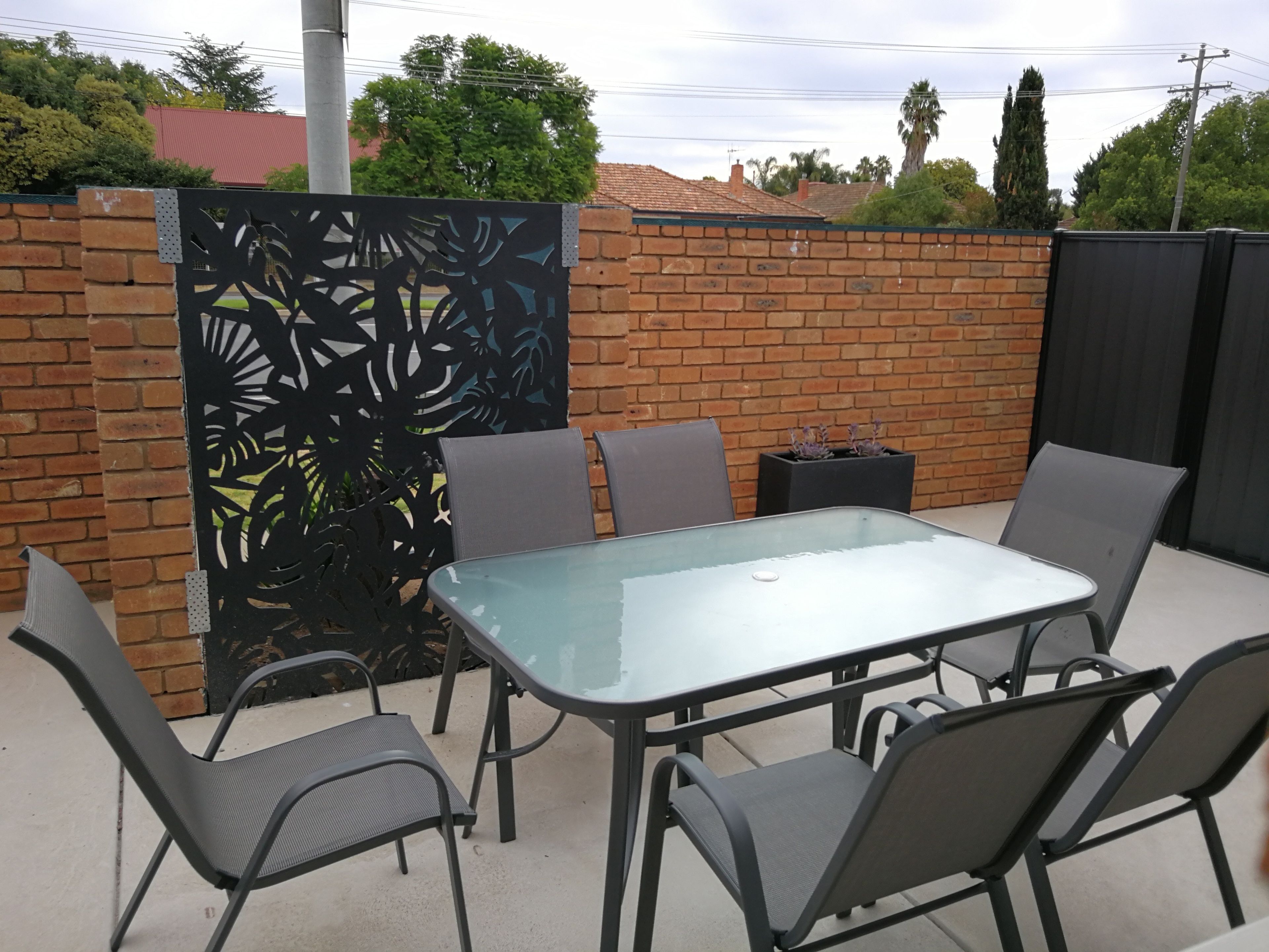 Um pátio externo com mesa de vidro e quatro cadeiras.