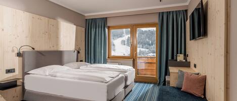 Quarto de hotel com cama, sofá, televisão e janela com vista para uma paisagem nevada.