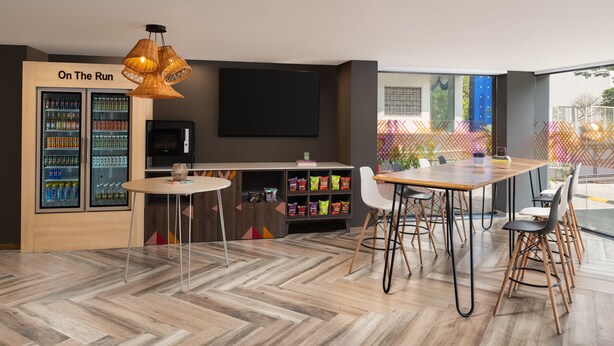 Um interior moderno com piso de madeira em padrão herringbone, área de bar de madeira com televisão e um espaço de estar com vista panorâmica pela janela.