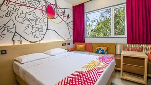 Quarto de hotel com uma cama grande, um mural com mapa na parede, uma janela com cortinas vermelhas e uma mesinha de cabeceira de madeira.