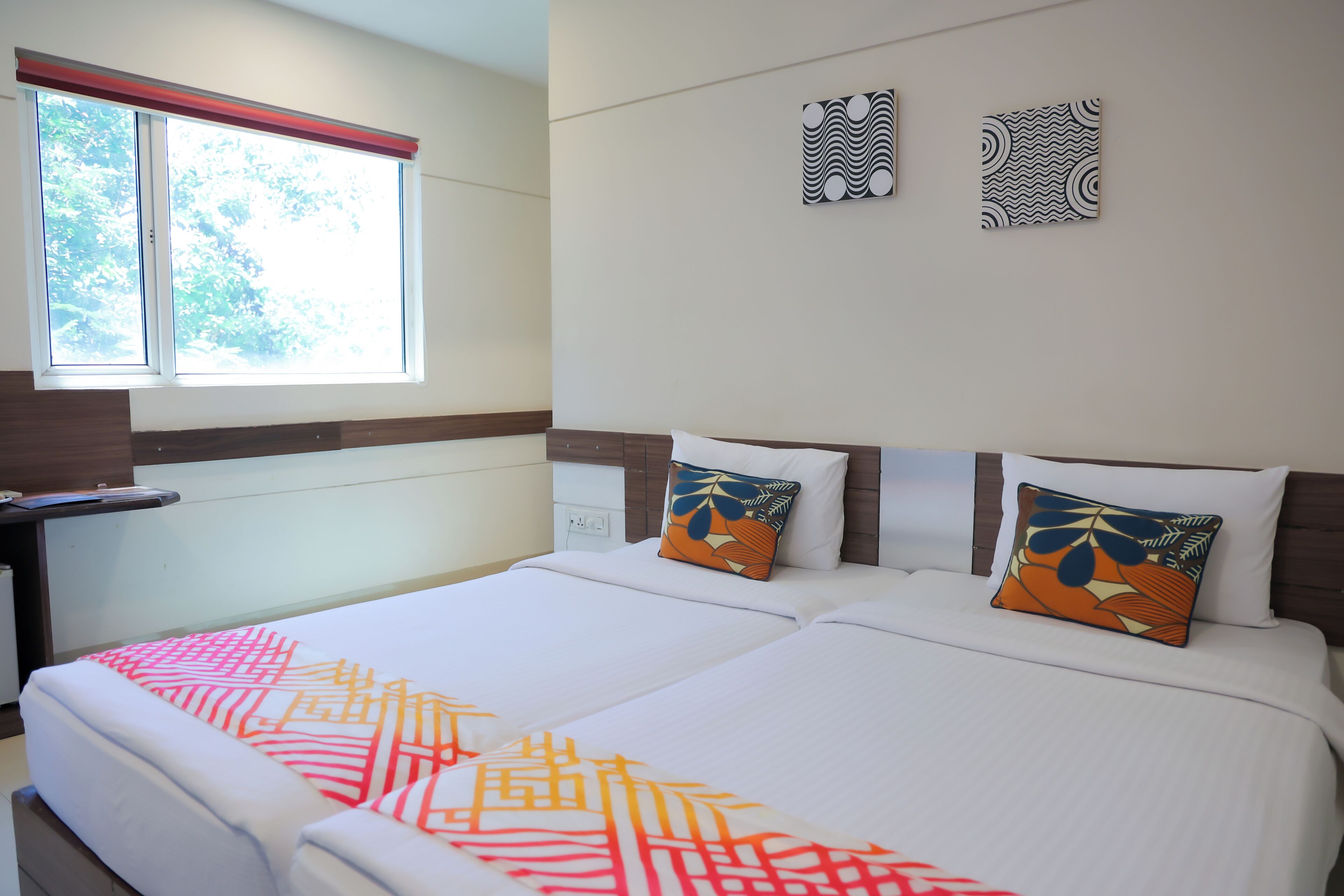 Quarto de hotel com uma cama grande, duas almofadas, uma mesa de cabeceira, uma janela e decoração na parede.