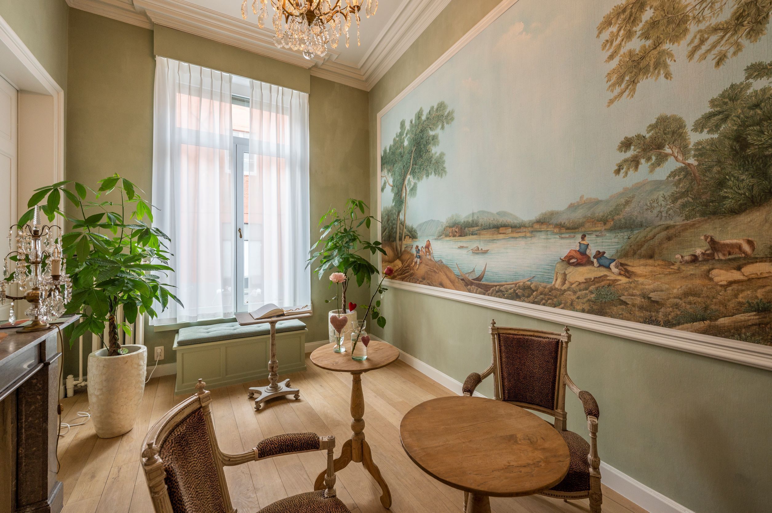 Uma sala de jantar com um grande mural, móveis de madeira e um candelabro.