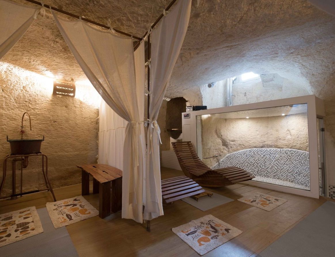 Um quarto com parede de pedra, uma cadeira suspensa, uma pequena mesa de madeira e um banco.
