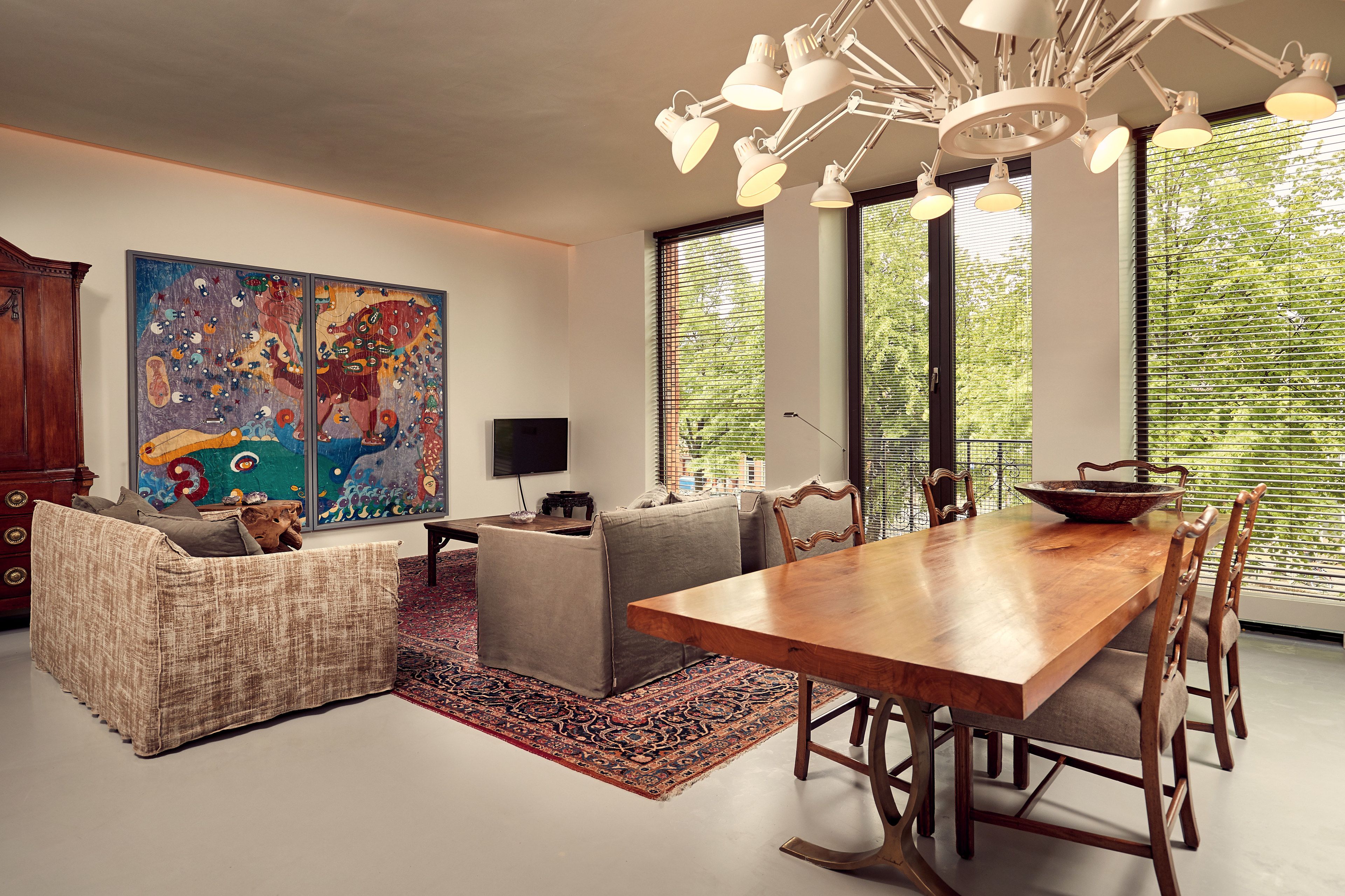 Uma sala de estar moderna com uma mesa de jantar de madeira, dois sofás, um quadro grande e uma televisão.