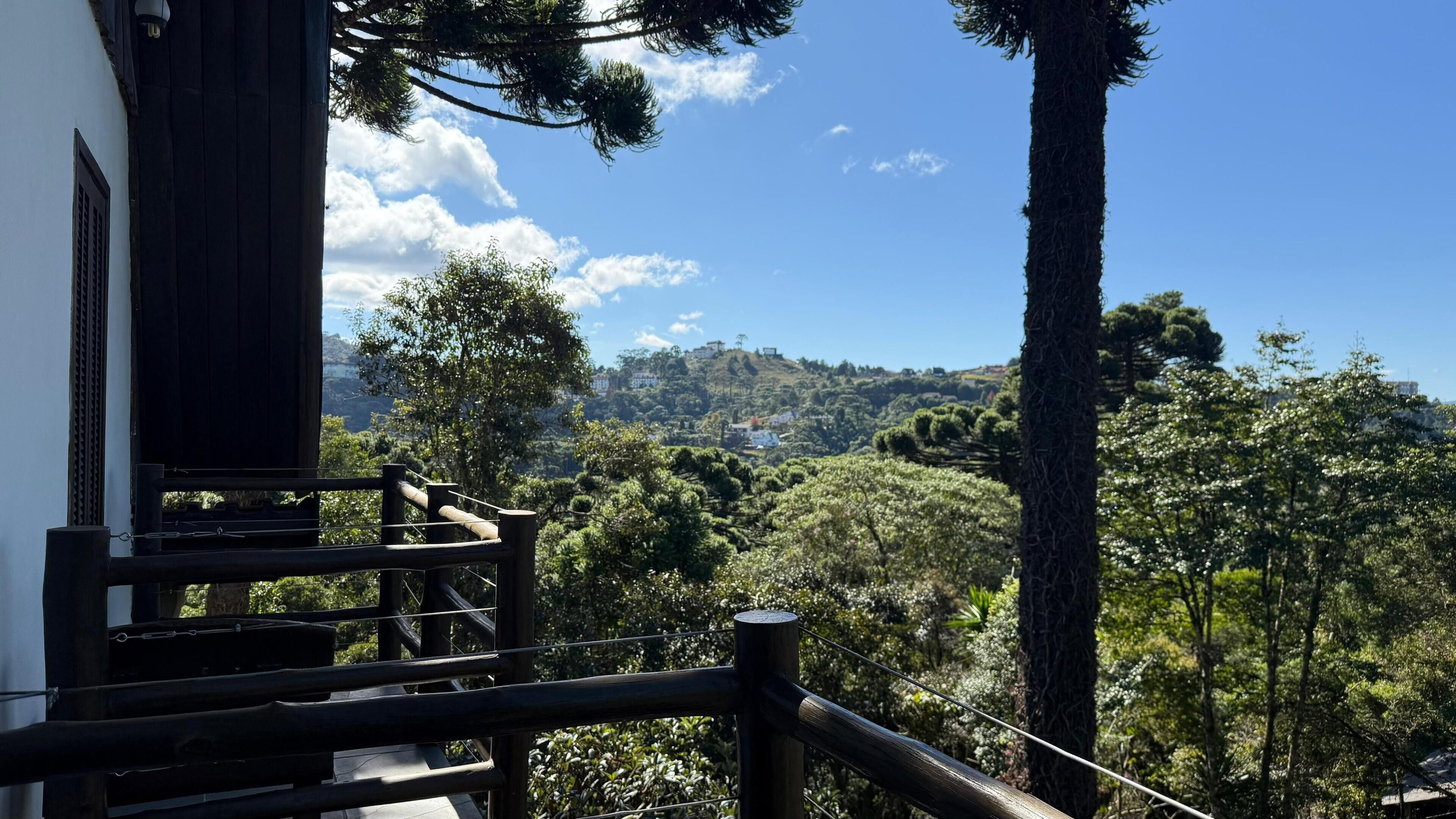 Uma varanda de madeira com vista para uma paisagem verdejante e edifícios ao longe.
