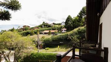 Vista de uma varanda com vista para uma encosta onde se veem algumas casas, um cercado de madeira e um céu claro.