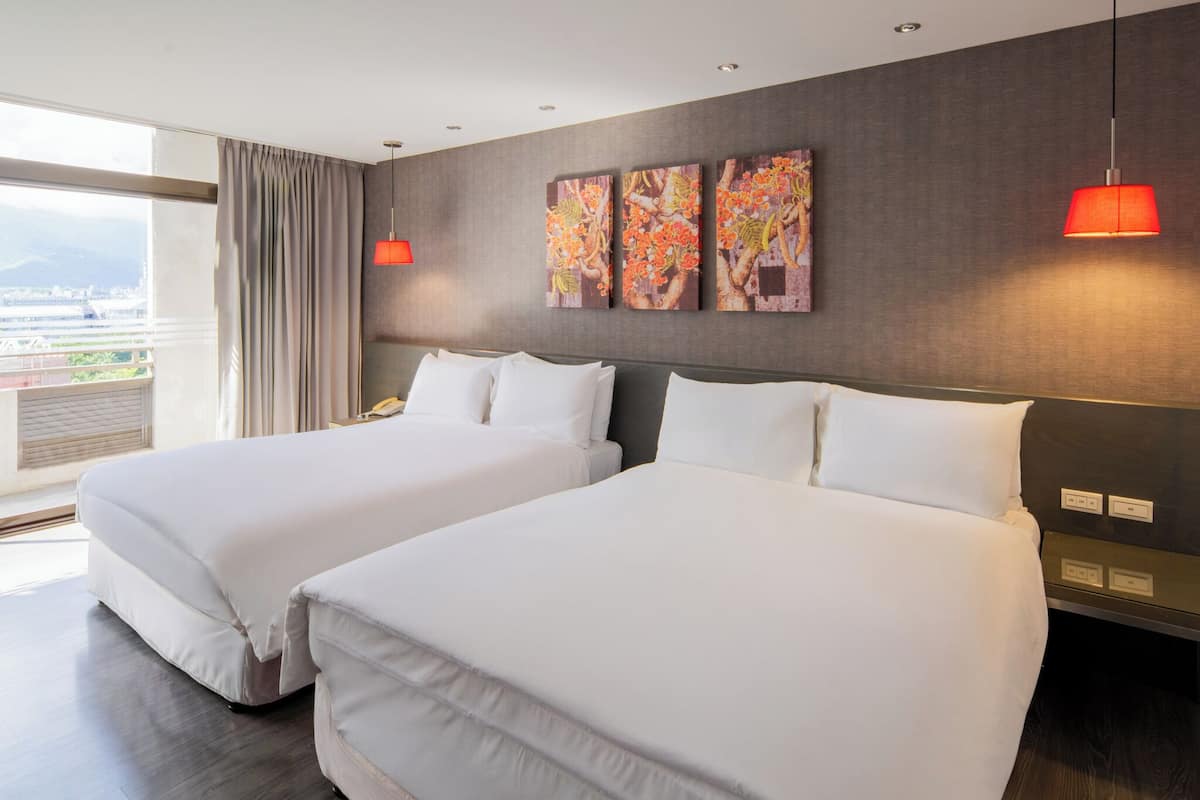 Quarto de hotel com duas camas, uma janela grande com cortinas e obras de arte na parede.