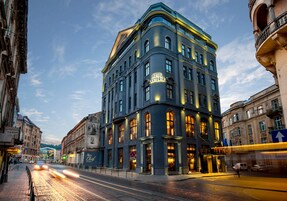 Um hotel histórico com arquitetura europeia clássica, destacando-se por sua localização de esquina, amplas janelas e fachada bem iluminada.