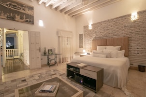 Quarto com uma cama grande, cabeceira de madeira, parede de tijolos decorativa, mesa pequena com abajur e mesa de centro de vidro.