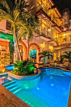 Uma área de piscina interna luxuosa com arco de tijolos, palmeiras e varanda em vários níveis com área de estar ao ar livre.