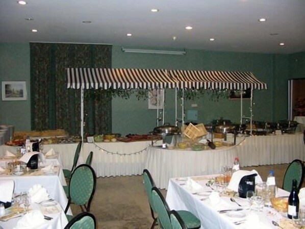 Salão de festas com mesas preparadas para refeição, área de buffet e toldo listrado.