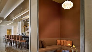Um hall moderno com um balcão de recepção extenso, uma área de estar com um sofá e poltronas, e um bar ao fundo.