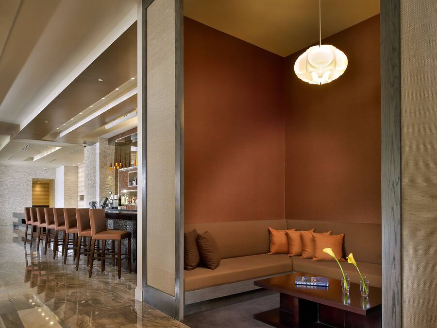 Um hall moderno com um balcão de recepção extenso, uma área de estar com um sofá e poltronas, e um bar ao fundo.