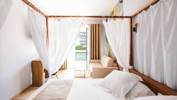 Quarto com cama, cabeceira de madeira, mesa de cabeceira de madeira, sofá bege e vista para o exterior.