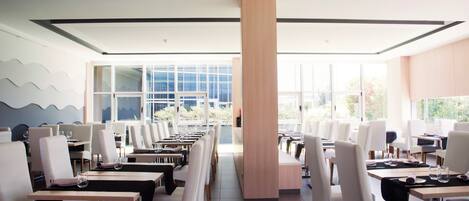 Um restaurante moderno com mesas comunitárias compridas e cabines individuais, grandes janelas com vista para a paisagem urbana.