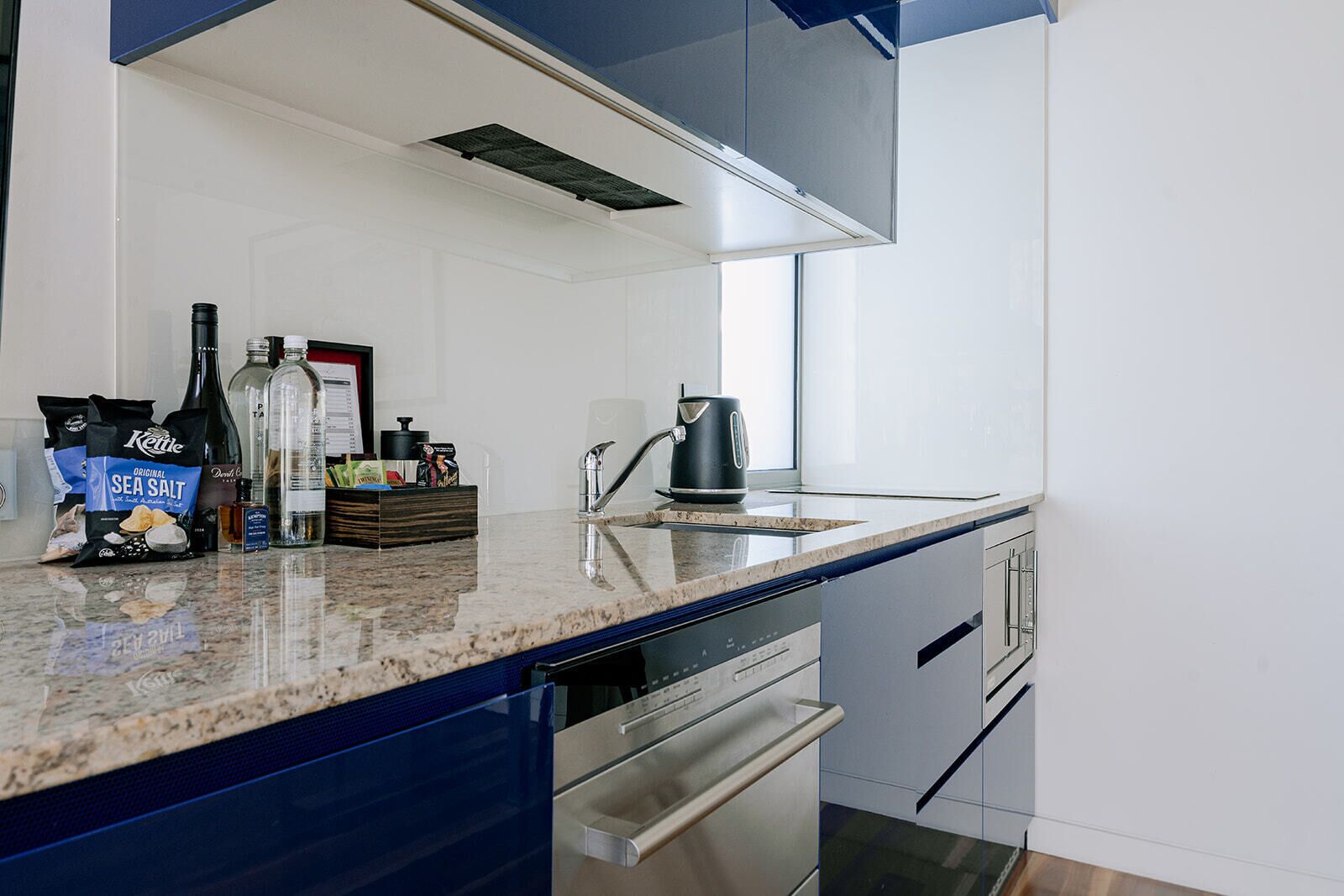 Cozinha moderna com bancada de granito, eletrodomésticos de aço inoxidável e chaleira preta.
