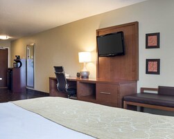 Quarto de hotel com cama, escrivaninha, cadeira, televisão e máquina de café.