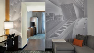 Quarto de hotel com design moderno, com uma escrivaninha, um sofá e vista para a paisagem urbana através de uma grande janela.