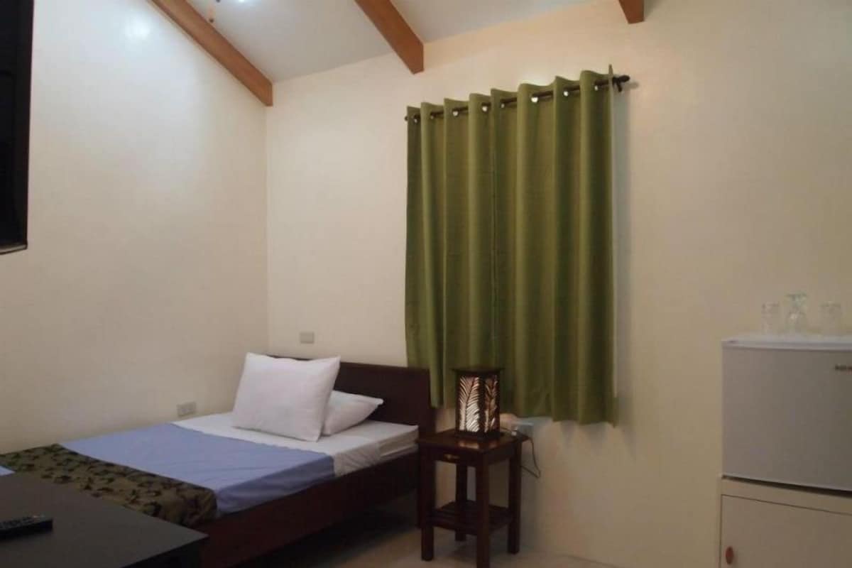 Um quarto pequeno e simples com uma cama, uma escrivaninha, uma cadeira e um frigorífico.