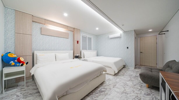 Quarto de hotel com duas camas, uma secretária pequena, uma cadeira e um guarda-roupa.