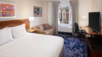Quarto de hotel com uma cama grande, um sofá, uma mesa com computador e uma televisão.
