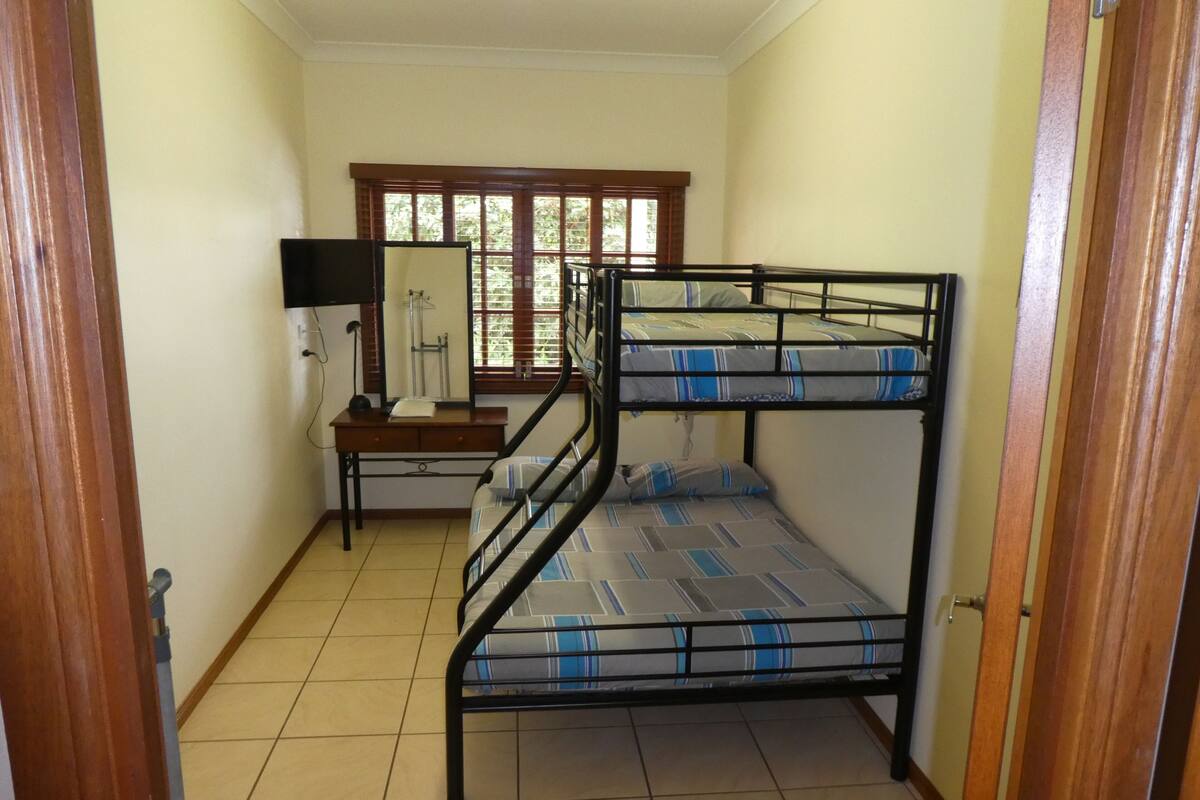Um quarto em dormitório com beliches, escrivaninha, cadeira e janela.