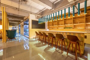 Uma área de bar com um balcão comprido, vários banquinhos e prateleiras com copos.