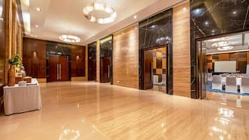 Um amplo hall de hotel com piso de mármore polido, painéis de madeira e um grande lustre.