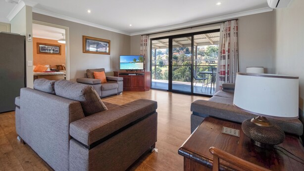 Sala de estar moderna com sofá, mesa de centro e TV. Possui varanda com vista para o exterior.