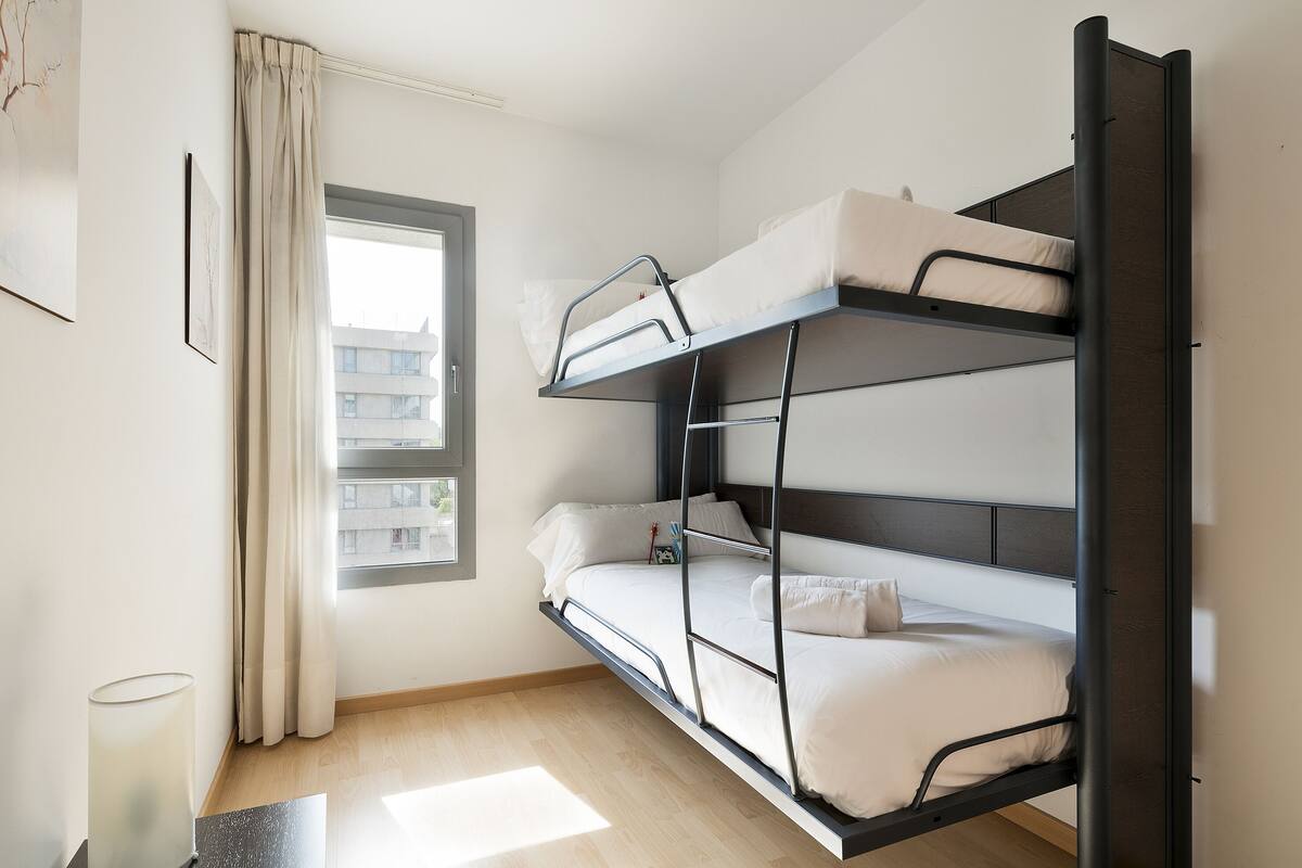 Quarto com beliche, janela, cortinas e abajur.