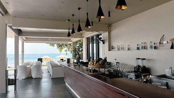 Uma área de bar moderna com vista para o oceano, mobiliário de vime branco e diversos utensílios e garrafas de bar.