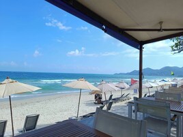 Um restaurante à beira-mar com mesas ao ar livre, guarda-sóis e vista para o oceano.