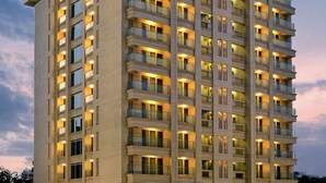 Um hotel de vários andares com varandas, entrada fechada por portão e fachada bem iluminada.