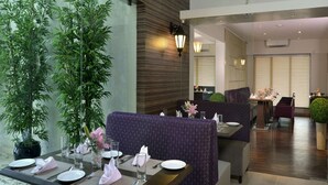Restaurante com mesas preparadas para refeições, apresentando um interior moderno com plantas de bambu e assentos estampados.