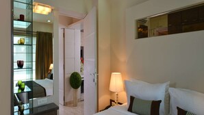 Quarto de hotel com uma cama grande, mesa de cabeceira com abajur, espelho e aparador com objetos decorativos.