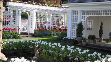Um jardim com um pérgola branca, um lago e diversas flores.