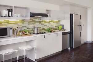 Uma cozinha moderna com armários brancos, uma geladeira de aço inoxidável e painel de azulejos.