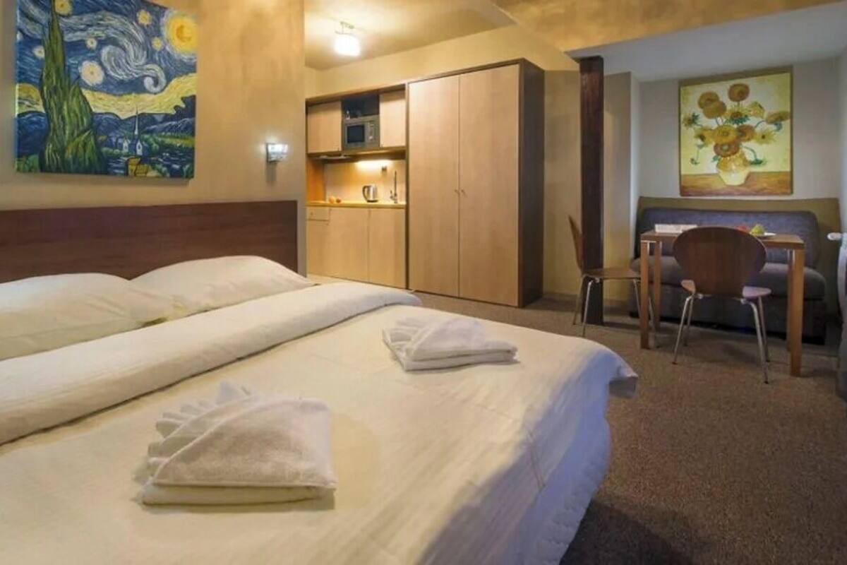 Quarto de hotel com cama de casal, uma kitchenette compacta, secretária com cadeira e obras de arte nas paredes.